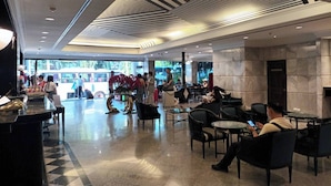 Um hall amplo com design de teto moderno, piso de mármore e área de estar com mesas e cadeiras.