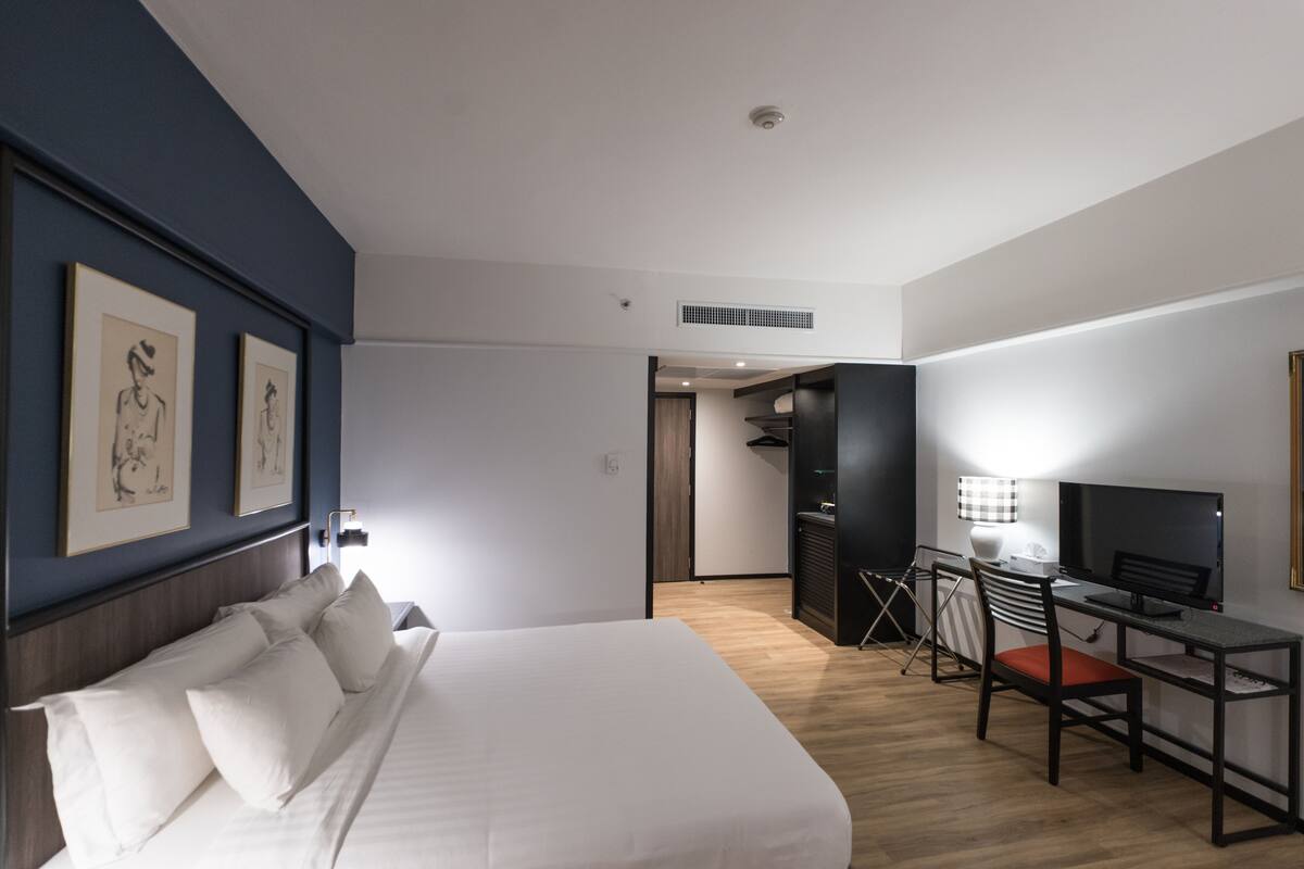 Quarto de hotel moderno com uma cama grande, uma escrivaninha com cadeira, televisão e obras de arte nas paredes.