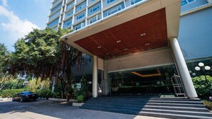 Entrada de um hotel moderno, com galeria coberta, grandes janelas e um carro estacionado próximo.