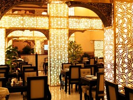 Uma sala de jantar com mesas e cadeiras, luminárias elaboradas e um papel de parede estampado.