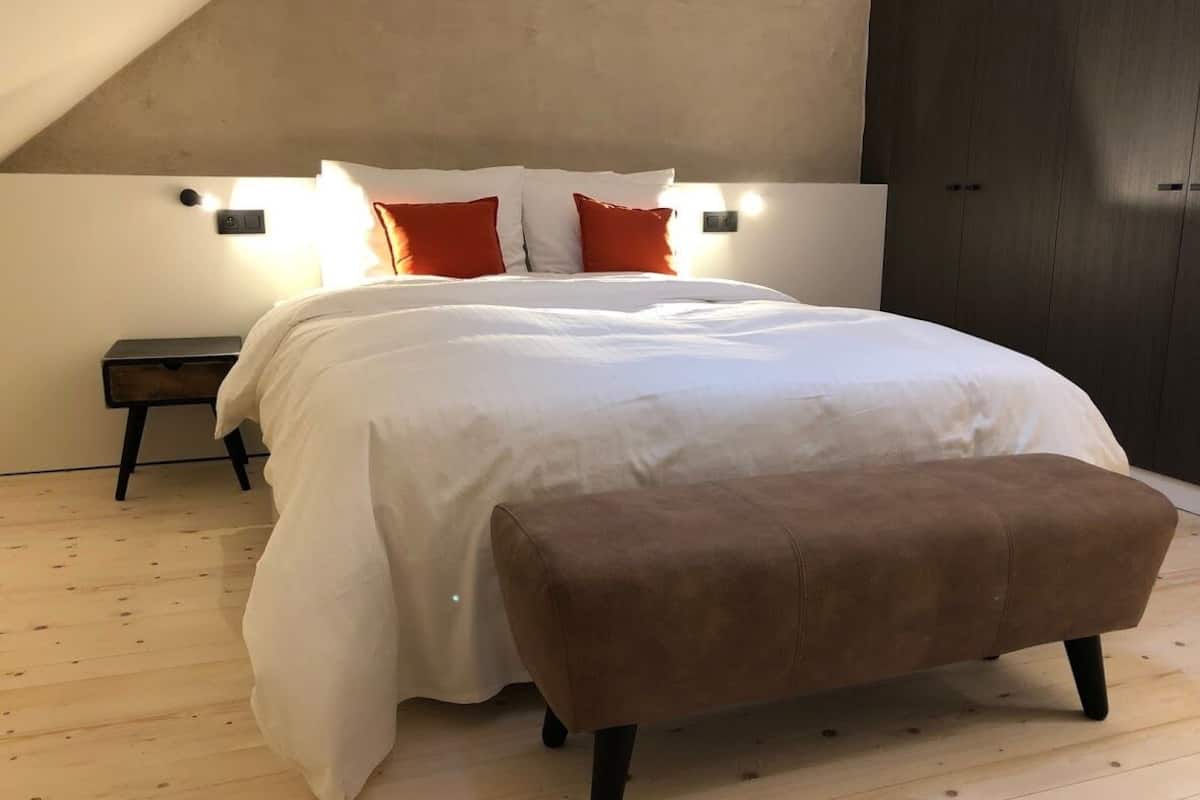Um quarto com uma cama grande, um banquinho e uma mesinha de cabeceira.