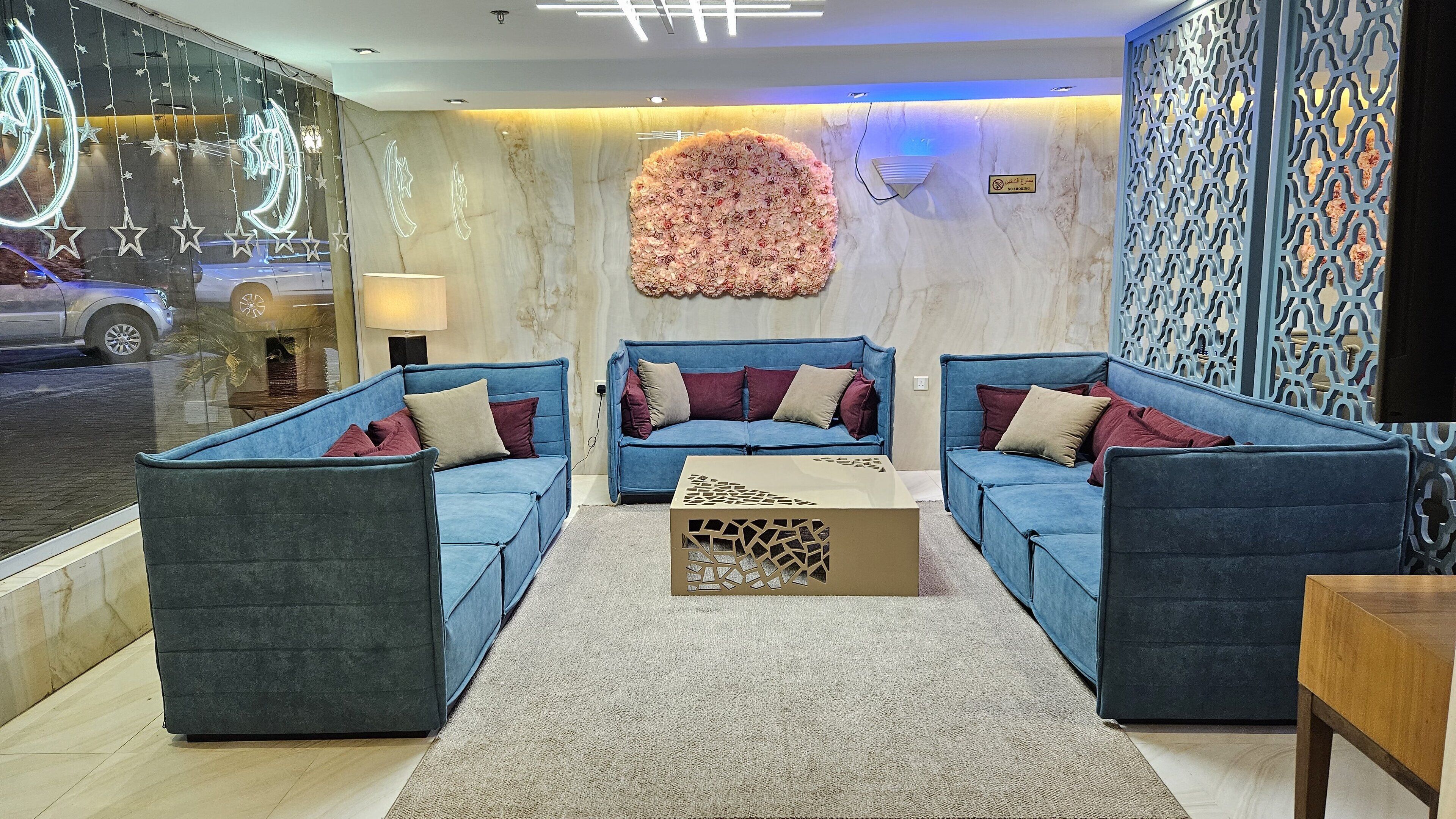 Uma sala de estar moderna com dois sofás azuis, uma mesa de centro e uma parede decorativa com um arranjo floral.