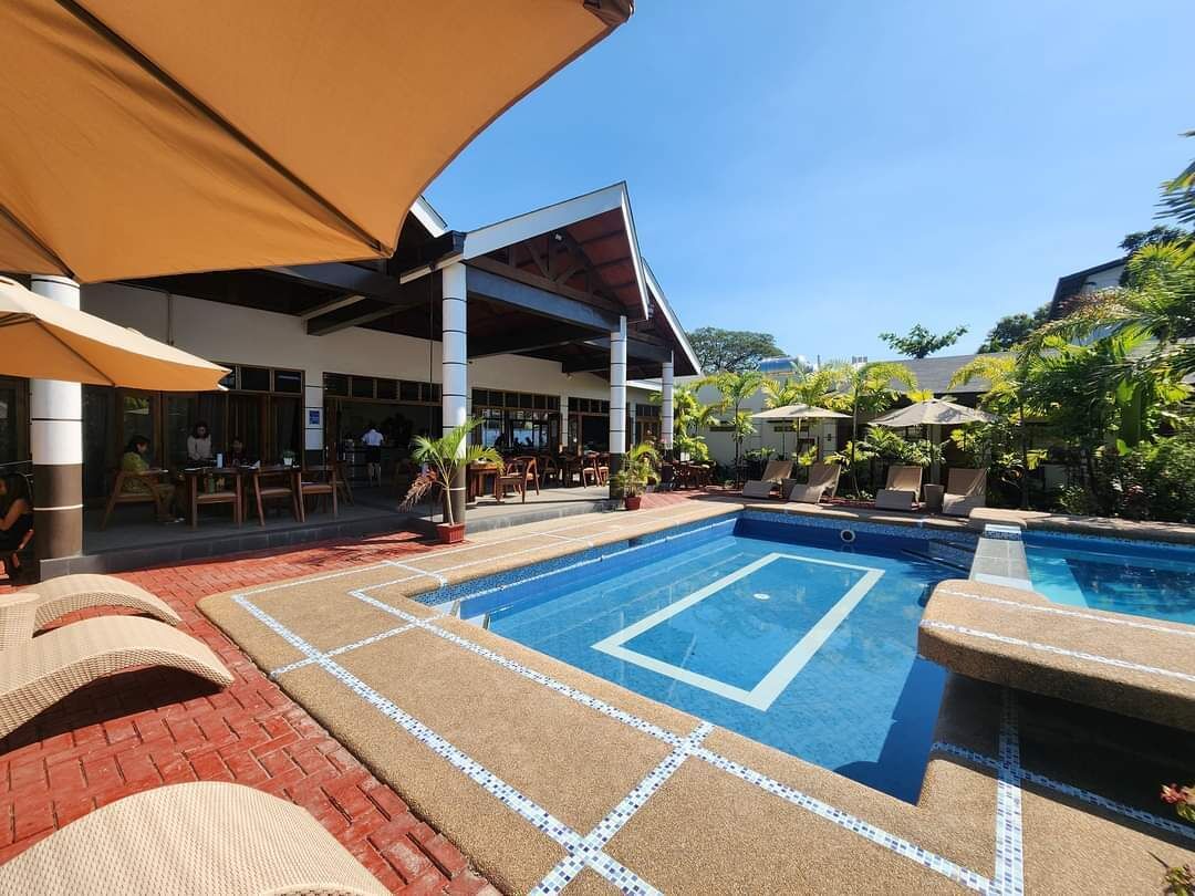 Uma piscina com espreguiçadeiras, guarda-sóis e um deck revestido em azulejos.