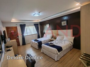 Quarto Deluxe Duplo com duas camas, uma escrivaninha, uma cadeira, janela com cortinas e iluminação no teto.