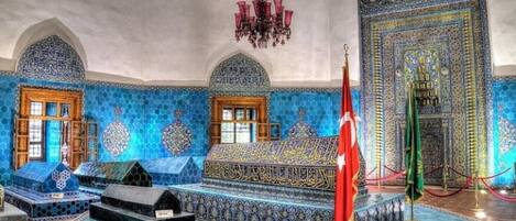 Um quarto com um tapete grande e ornamentado, um candelabro e uma bandeira.