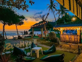 Um bar à beira-mar com área externa para sentar, uma placa com a inscrição '2UHY6I' e vista para o oceano ao pôr do sol.