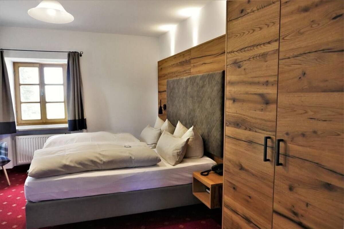 Quarto com cama, mesa de cabeceira, guarda-roupa e janela com cortinas.