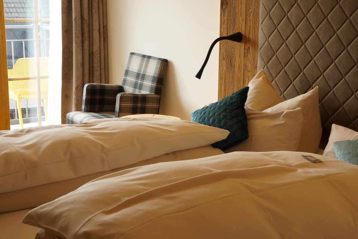 Quarto de hotel com cama, almofadas, uma cadeira e janela com cortinas.