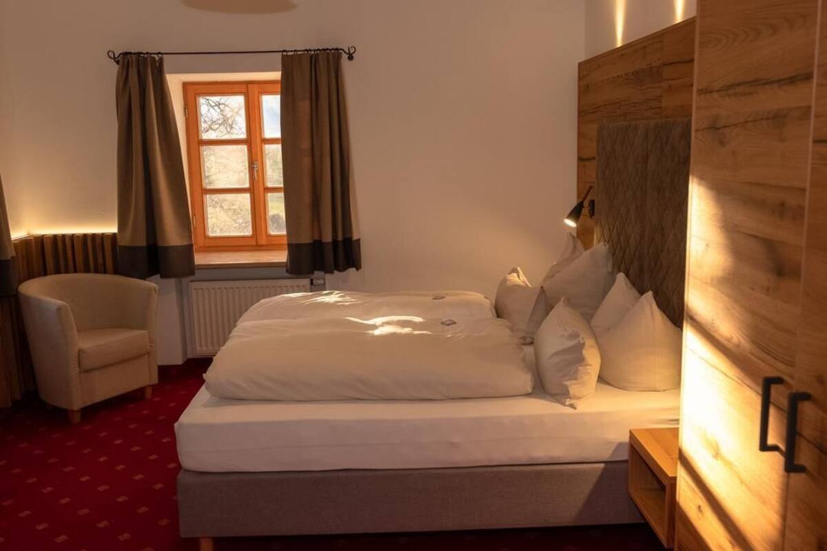 Um quarto com cama, uma cadeira, um guarda-roupa de madeira, uma janela com cortinas e um radiador.