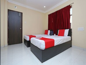 Quarto de hotel com duas camas, roupa de cama vermelha e branca, cabeceira escura, cortina vermelha e piso de azulejos brancos.