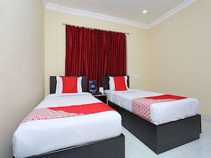 Quarto de hotel com duas camas, cada uma com roupa de cama branca e detalhes vermelhos, uma cortina vermelha e teto branco.