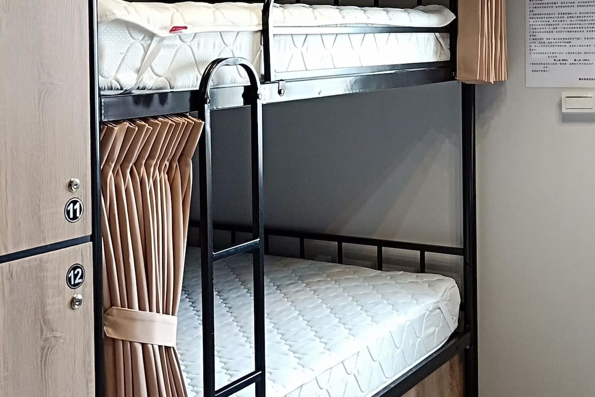Quarto com beliches, guarda-roupa de madeira, cortina e interruptor na parede.