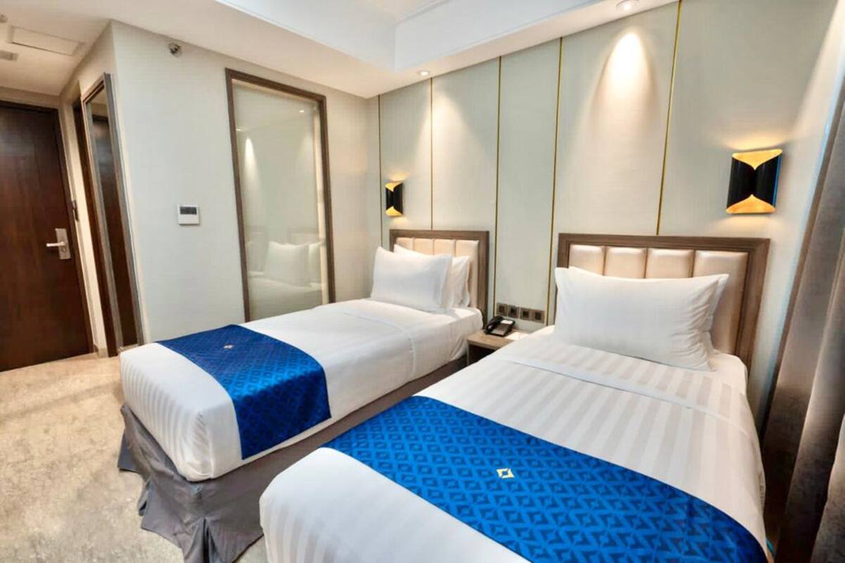 Quarto de hotel com duas camas, um espelho, mesa de cabeceira com telefone e uma porta.