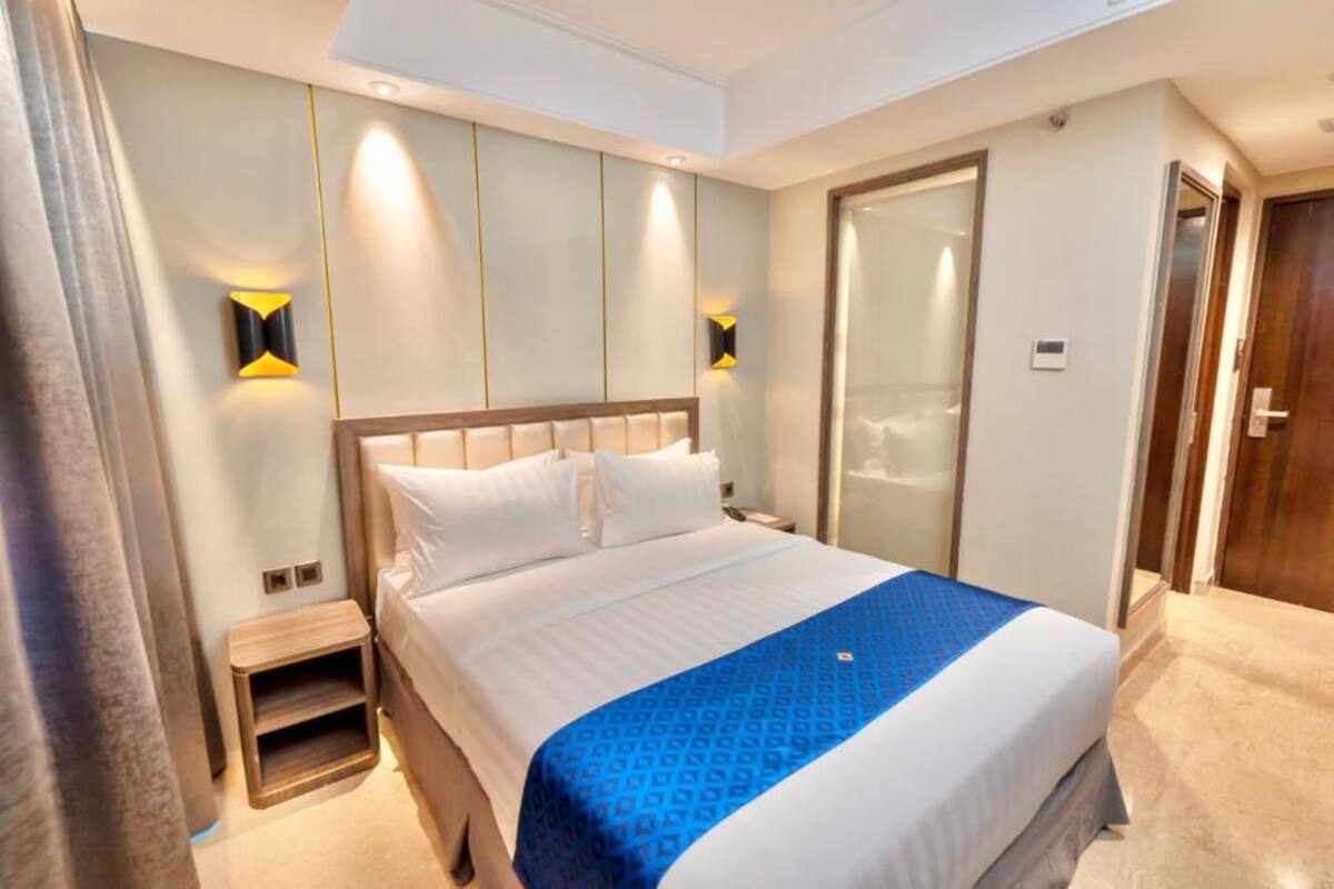 Quarto de hotel com uma cama grande, duas mesas de cabeceira, guarda-roupa e um armário com portas deslizantes.