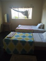 Quarto com duas camas, uma mesinha e janela com vista para o verde.