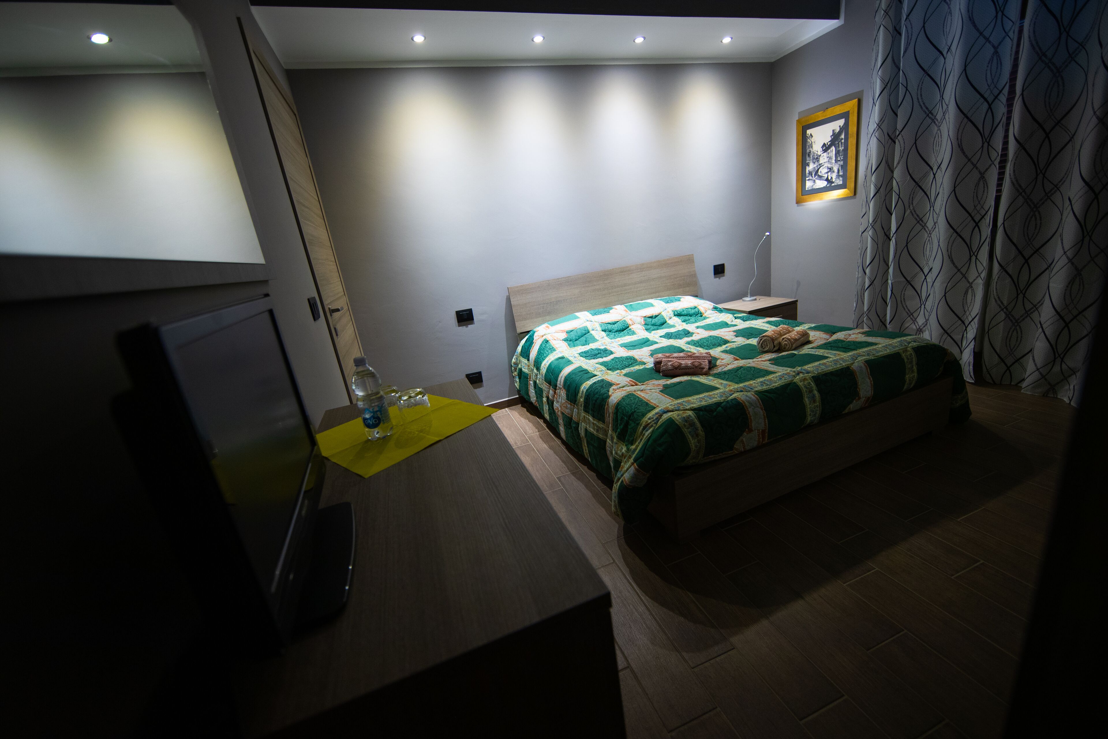 Quarto com cama, mesa de cabeceira e televisão.