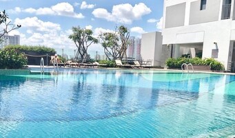 Piscina cristalina com espreguiçadeiras e um edifício moderno ao fundo.