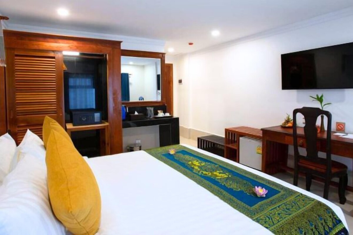 Quarto de hotel com cama, escrivaninha, televisão e espelho.