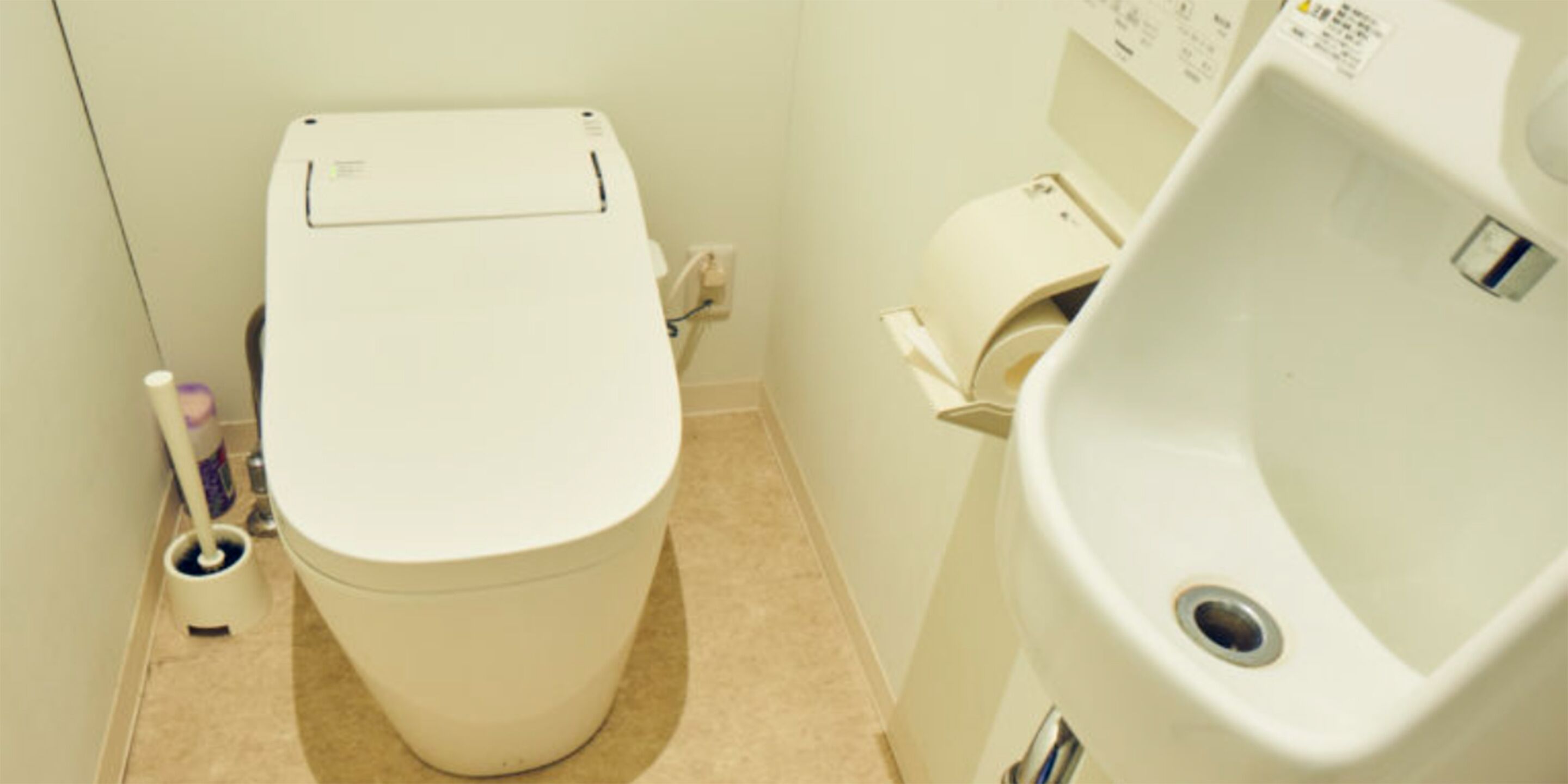 Casa de banho pequena e compacta, com sanita, lavatório e suporte para papel higiénico.