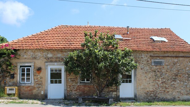Um edifício de pedra com telhado de telhas vermelhas, uma porta branca e uma pequena janela.