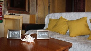 Um quarto aconchegante com uma mesa de madeira, dois quadros com palavras, uma cama com almofadas amarelas e uma janela com vista para o exterior.