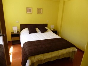 Quarto de hotel com uma cama, duas mesas de cabeceira e uma parede amarela.