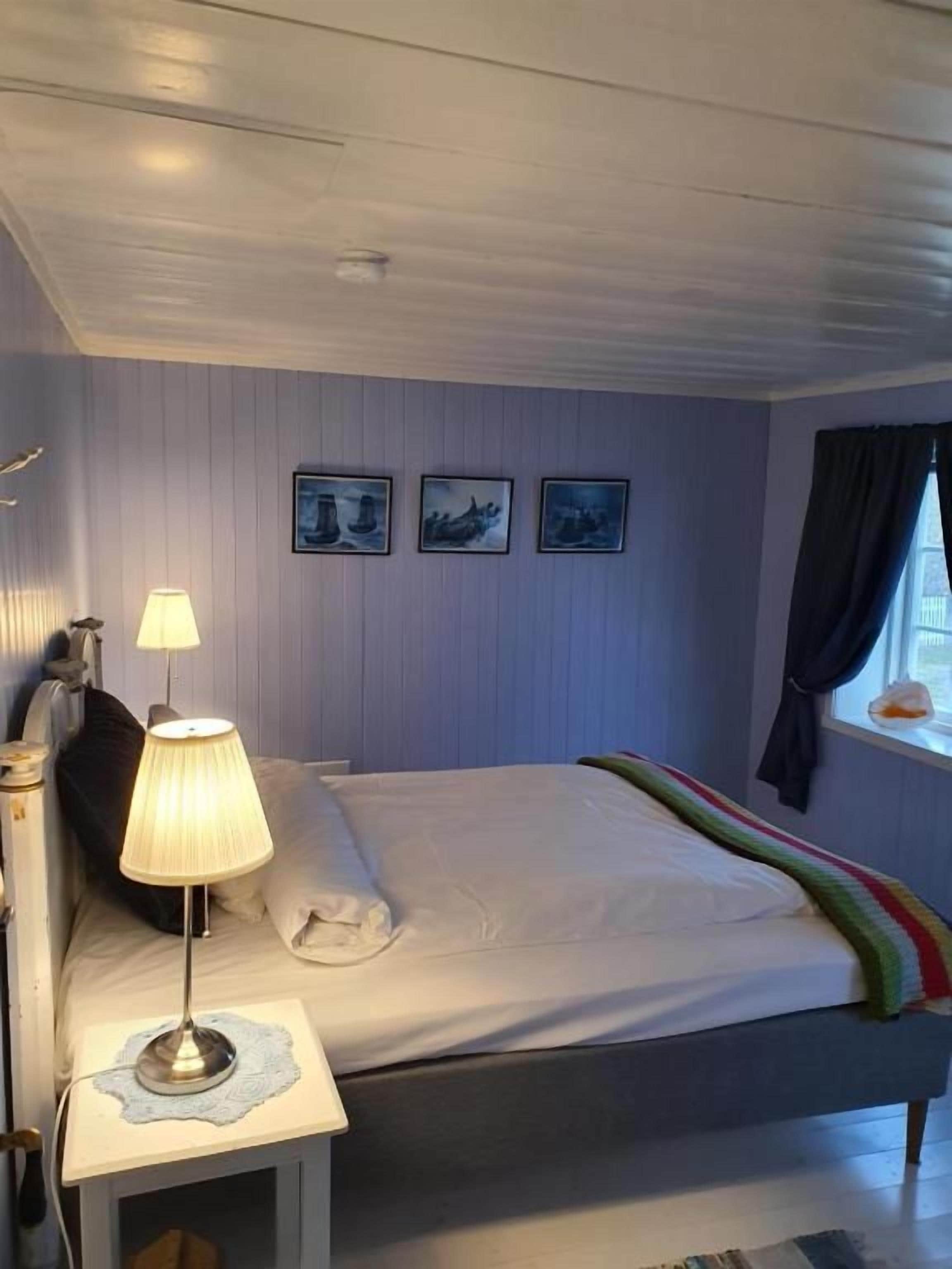 Quarto com cama, abajur e quadros na parede.