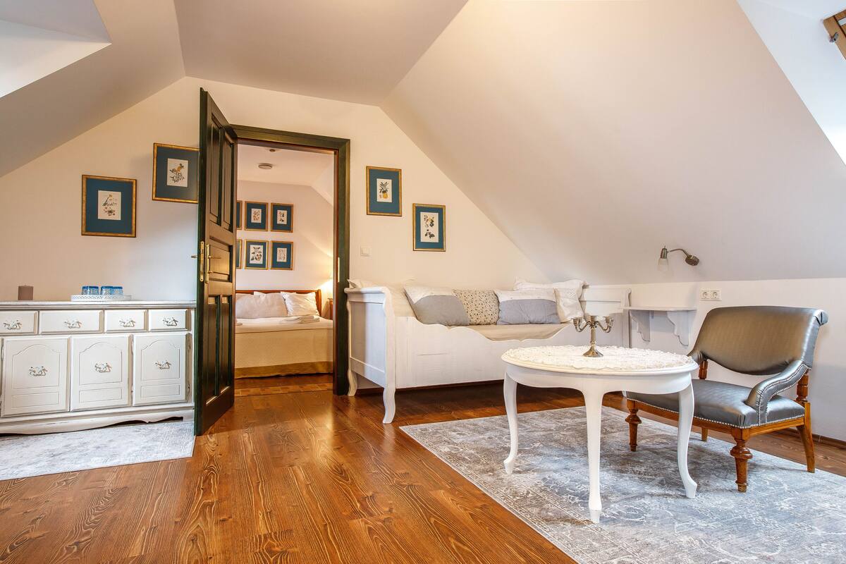 Quarto com sofá branco, cadeira de madeira, mesa branca e armário de madeira.