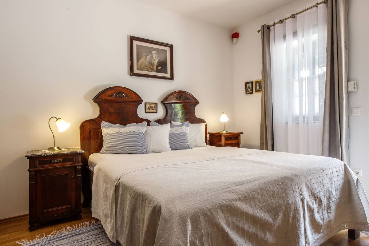 Quarto com cama grande, cabeceira de madeira, duas mesas de cabeceira com luminárias e um quadro na parede.