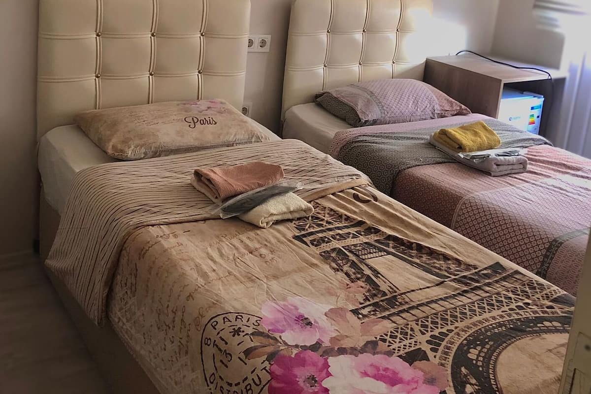 Quarto com duas camas, cada uma com cabeceira, mesa de cabeceira e abajur.