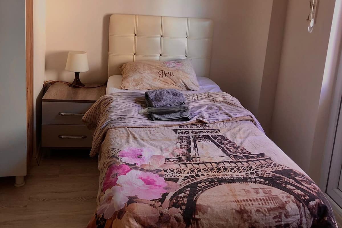 Quarto com cama, mesa de cabeceira, abajur, ar-condicionado e luminária na parede.