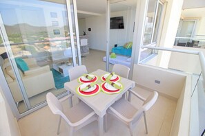 Um apartamento moderno com varanda, área de jantar com cadeiras e mesa brancas, e sala de estar com sofá e televisão.