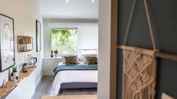 Quarto com cama, janela e um painel de macramé fixado na parede.