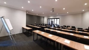 Uma sala de conferências com várias mesas e cadeiras, uma lousa branca e um projetor.