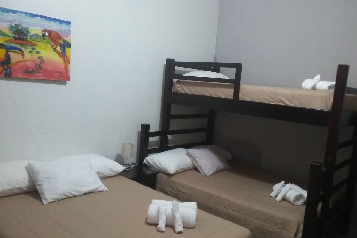 Quarto com beliches, dois colchões, cada um com travesseiro e toalha enrolada. Um quadro está pendurado na parede acima das camas.