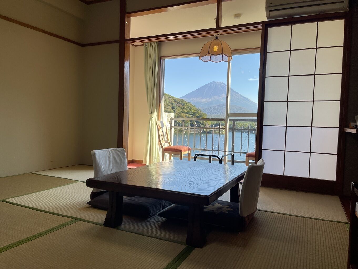 Um quarto japonês tradicional com tatames, uma mesa baixa e vista para uma montanha.
