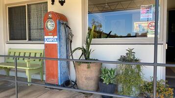 Uma bomba de gasolina AMPOL antiga em frente a um edifício com um banco verde e plantas em vasos.