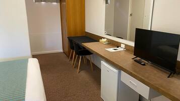Quarto de hotel pequeno com uma cama de solteiro, uma escrivaninha com televisão, um frigorífico compacto e um guarda-roupa de madeira.