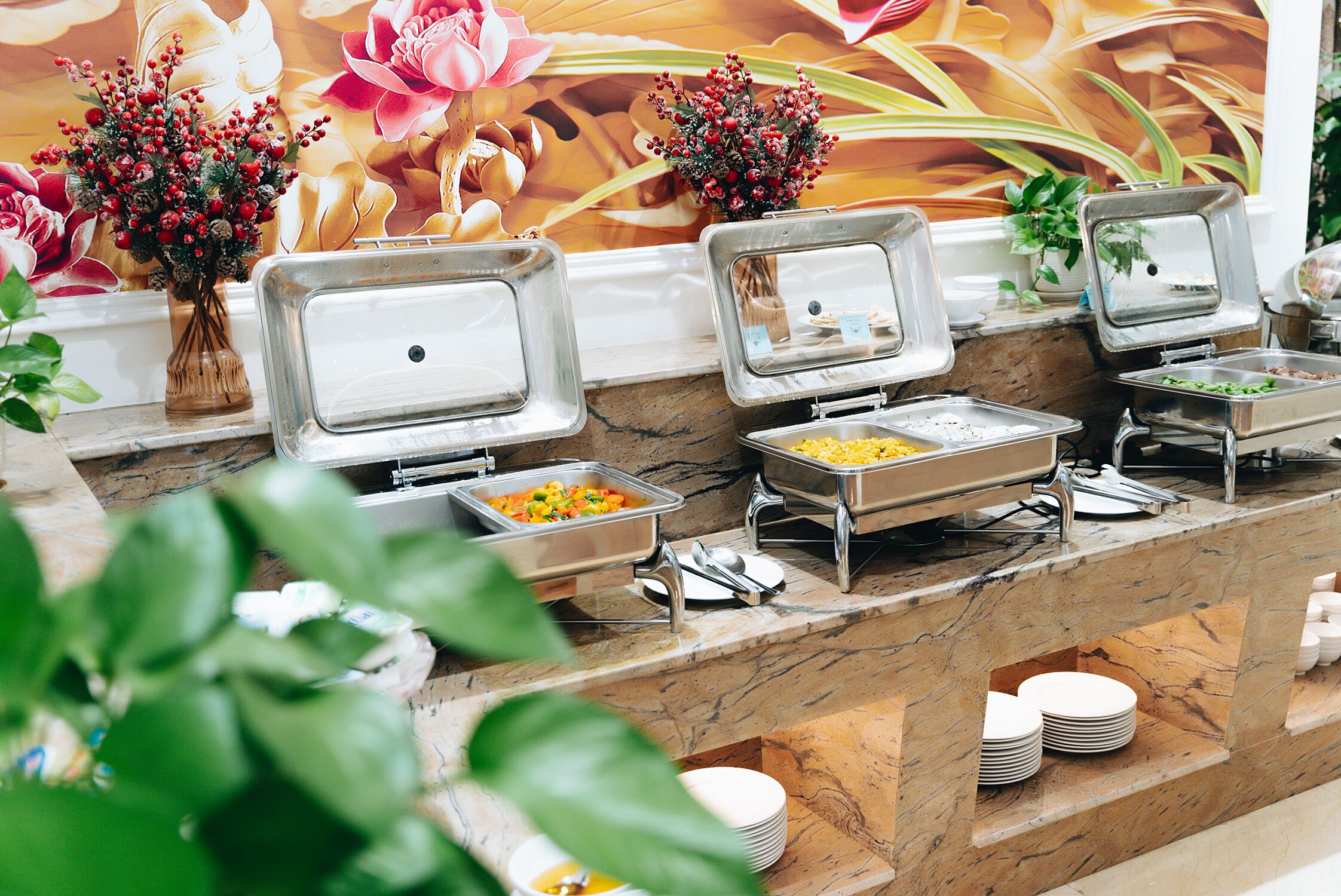 Disposição de buffet com várias estações de comida, bancada de mármore e um mural floral ao fundo.