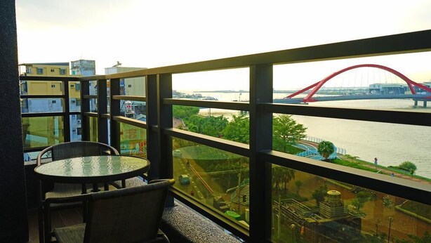 Uma varanda com vista para um rio e uma ponte vermelha. Há uma mesa e uma cadeira na varanda.