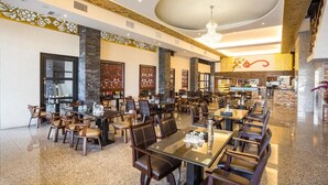 Um restaurante amplo com várias mesas e cadeiras, um candelabro e painéis decorativos na parede.