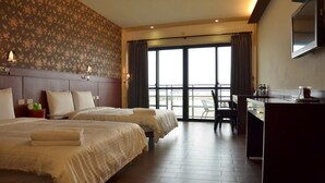 Quarto de hotel com duas camas, uma escrivaninha, uma cadeira, varanda com vista e uma janela grande.