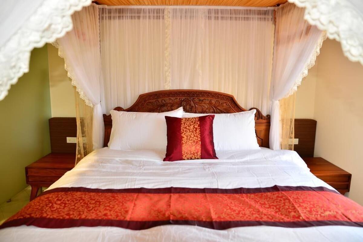 Cama com dossel, roupa de cama branca e almofada de destaque em vermelho e dourado.