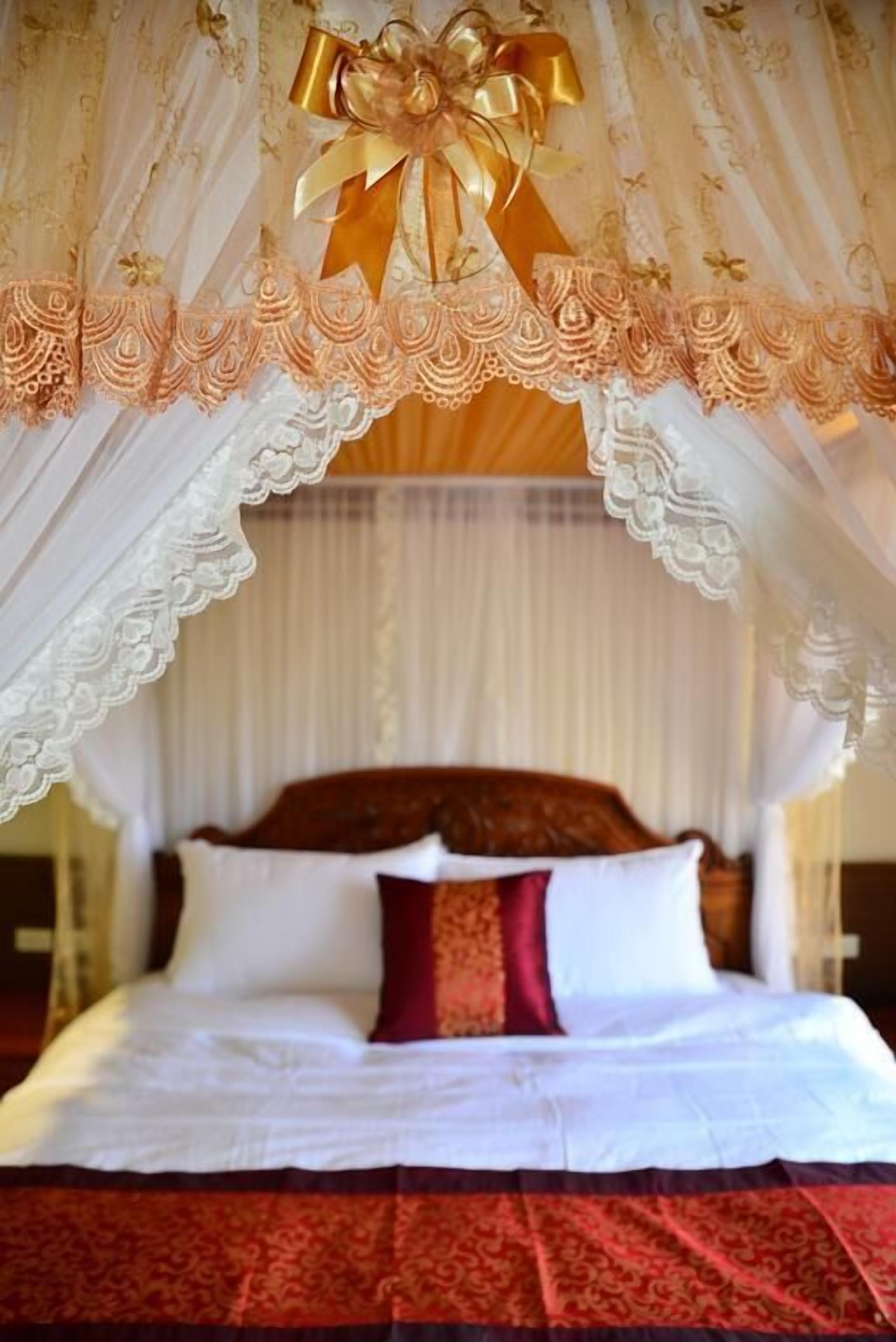 Uma cama com dossel, roupa de cama branca e colcha vermelha.