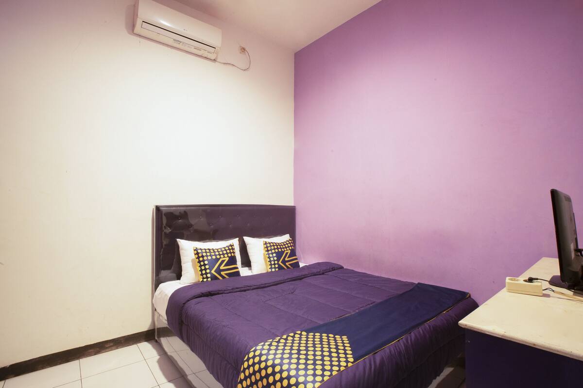 Um quarto com uma cama, uma escrivaninha com computador e ar condicionado na parede.
