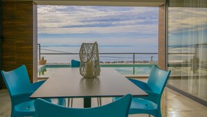 Uma varanda com mesa e cadeiras, um vaso decorativo e vista para o mar e uma ponte.