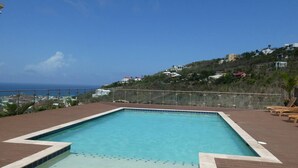 Piscina retangular com borda azulejada, rodeada por um deck de madeira.