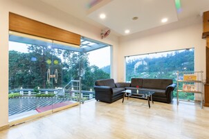 Ampla sala de estar com uma grande janela que oferece vista para um jardim exuberante e edifícios ao longe.