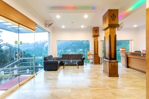 Um hall amplo com balcão de recepção, área de estar e parede de vidro com vista para o exterior.