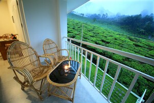 Varanda com cadeiras de vime e mesa, com vista para uma plantação de chá verde exuberante.